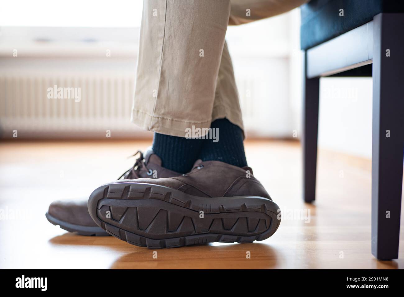 Unrecognizable man's crossed legs in causal pants and brown leather ...