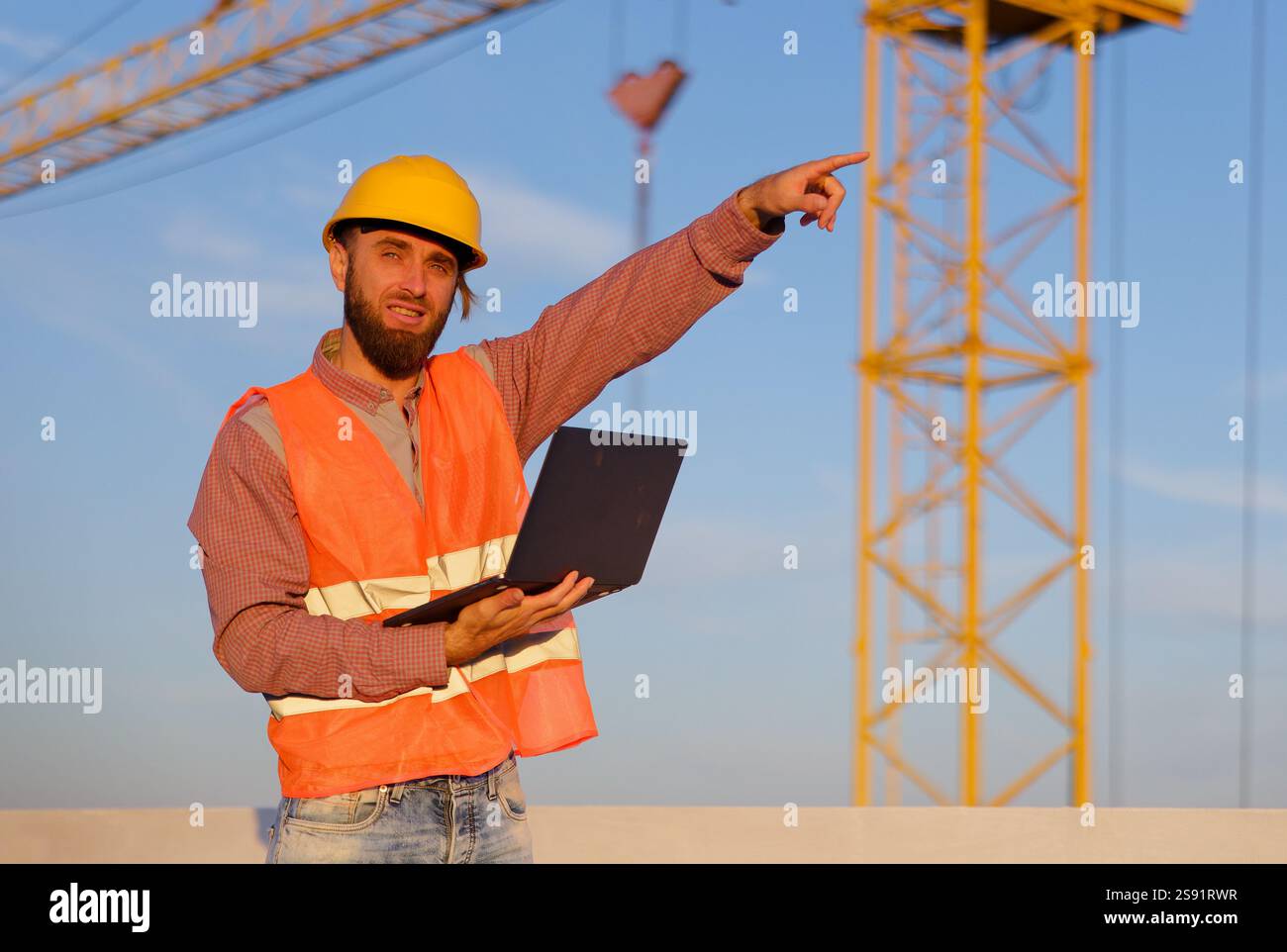 Construction engineer using laptop at building site with crane in ...
