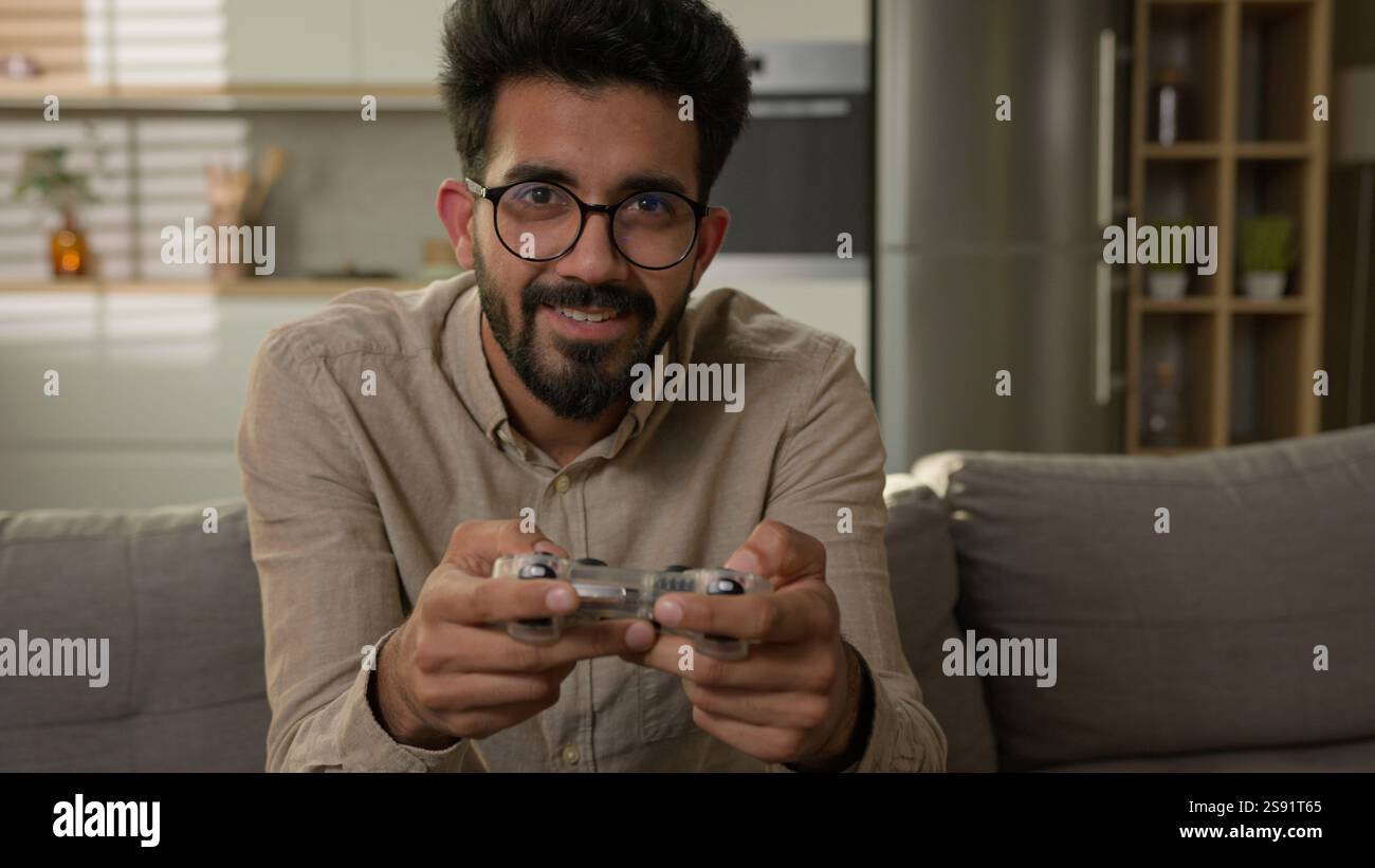 Arabian Indian man guy play video game at home kitchen on sofa male ...
