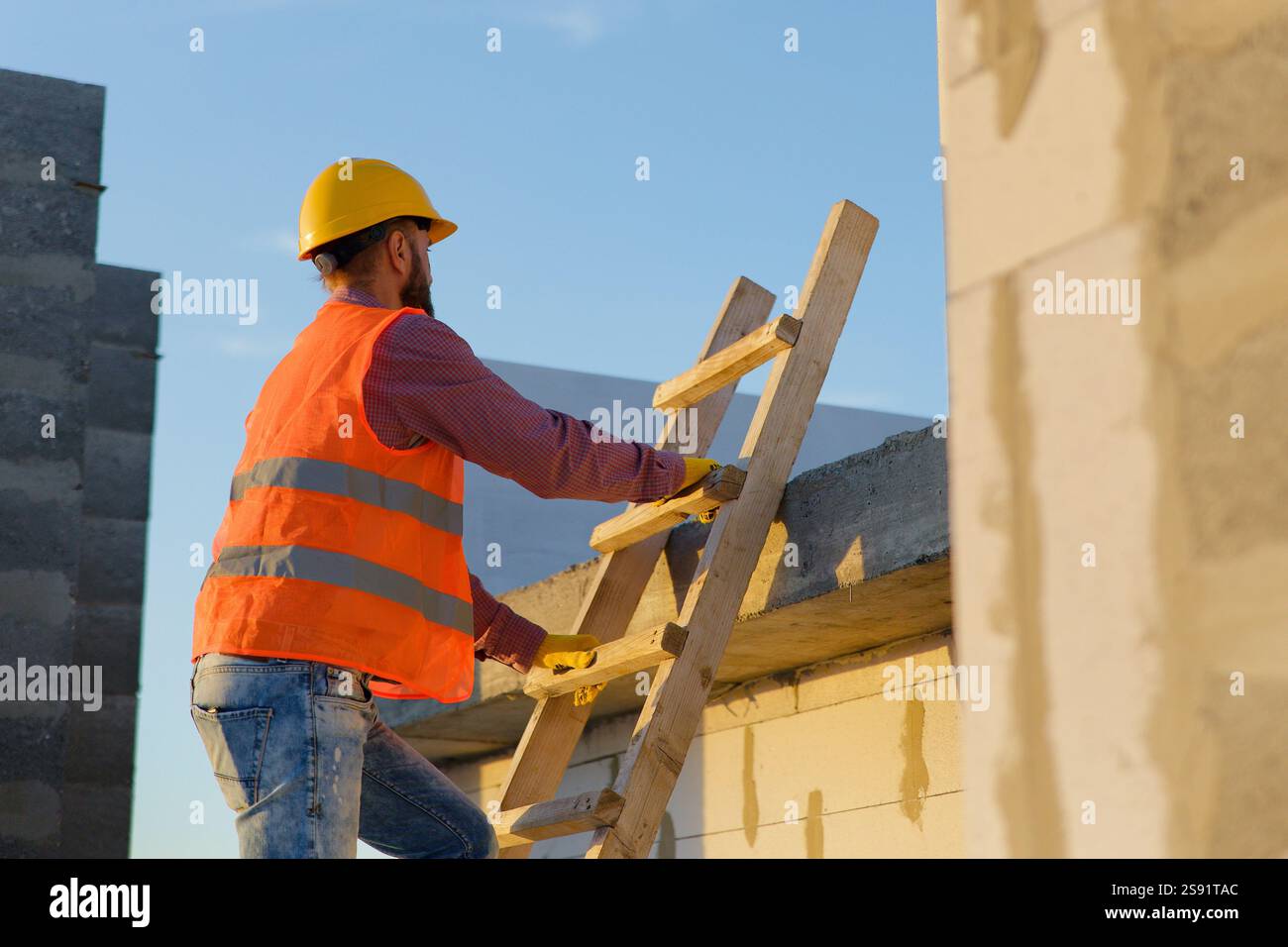Construction worker with safety helmet and vest climbing a wooden ...