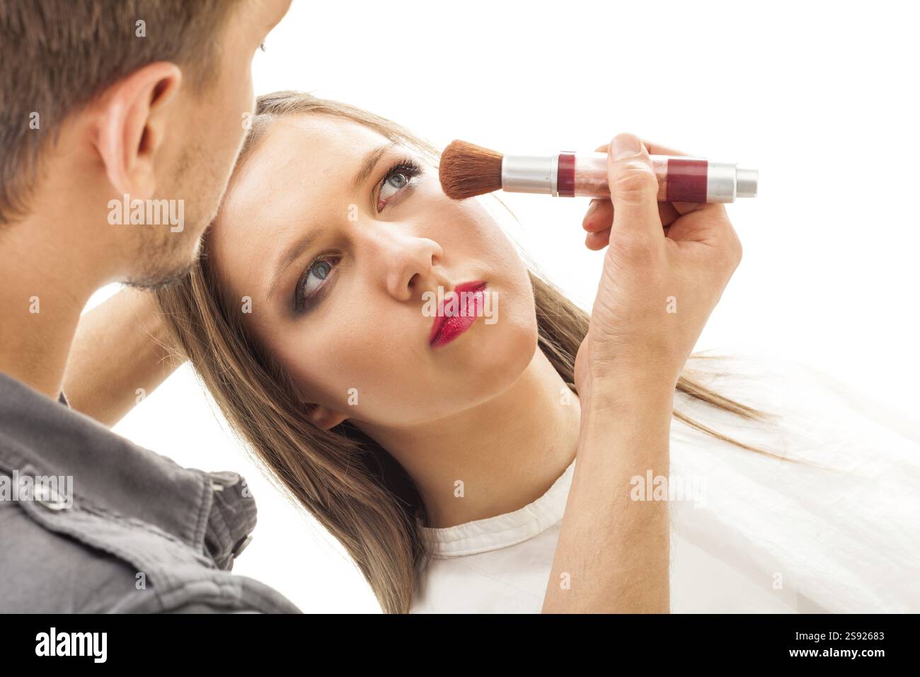 Make-up application. Make-up artist applies powder in front of a white ...