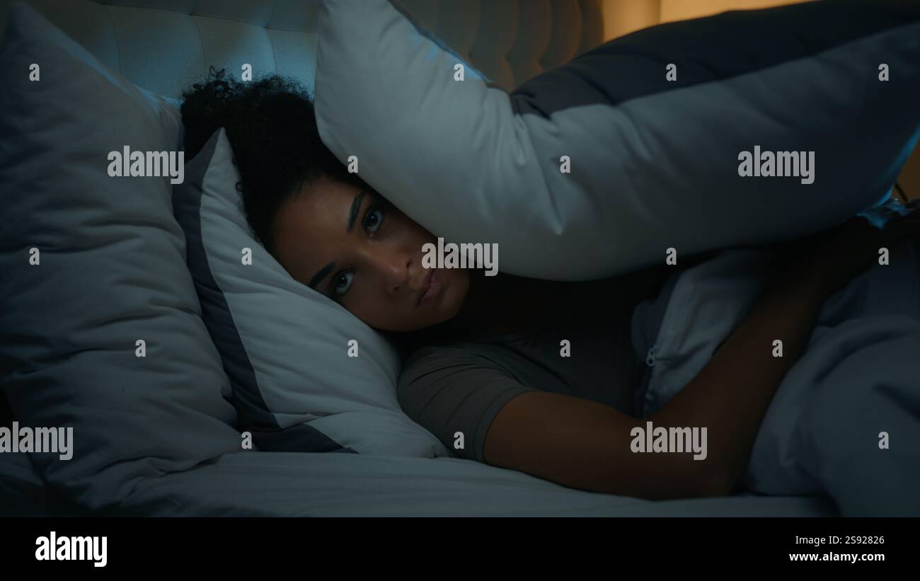 Noisy neighbours problem annoyed African American woman lying in bed ...