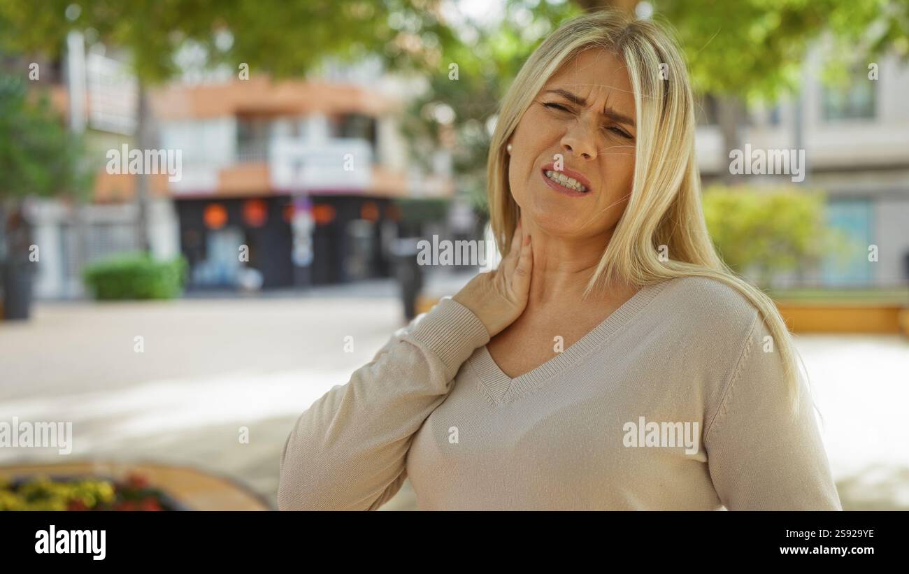 Woman with neck pain stands in an urban park with sunny weather ...