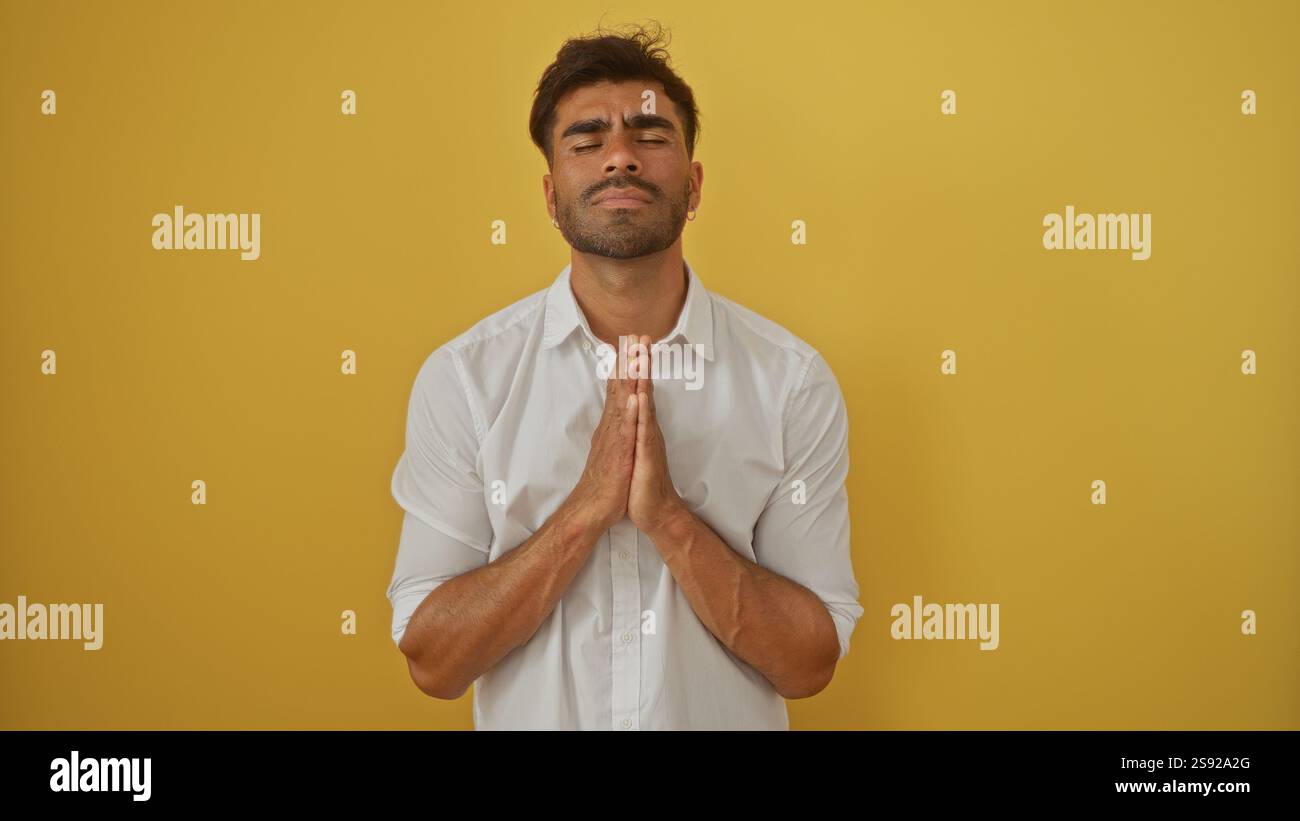 Young hispanic man in white shirt with hands in prayer position stands ...