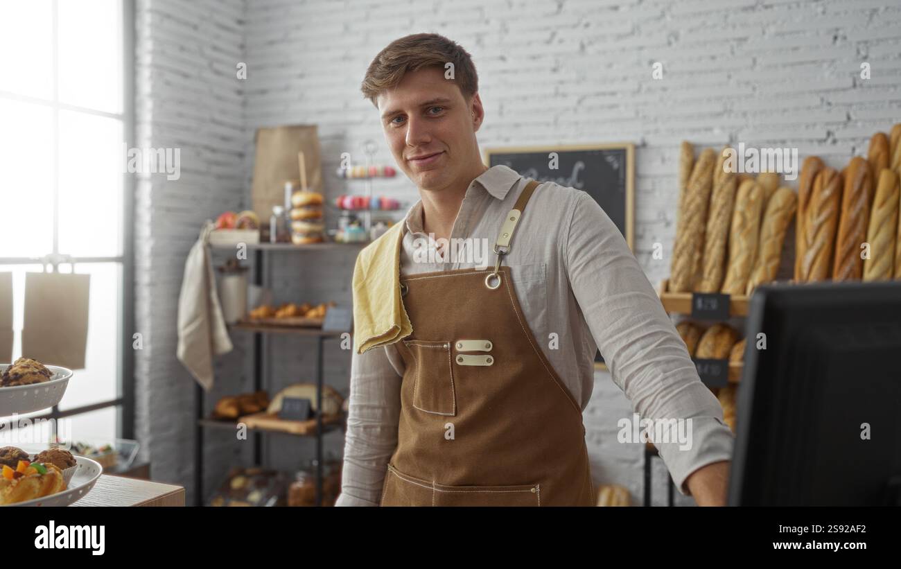 Young man wearing apron stands in bakery with shelves of bread and ...