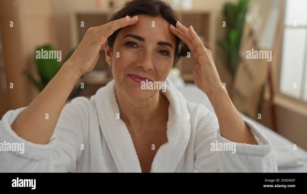 Woman in a spa wearing a white robe, touching her forehead, captured ...