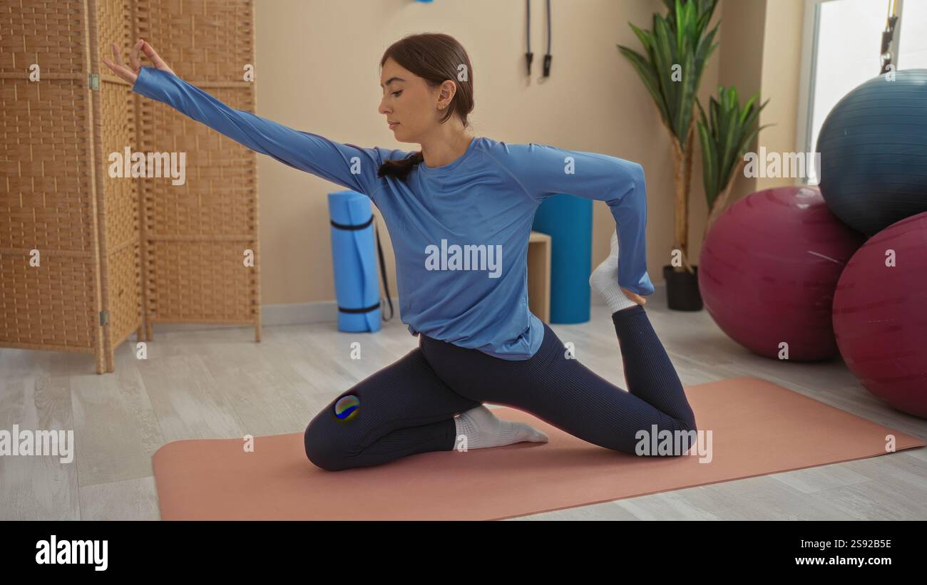 Young woman practicing stretching exercises indoors in a gym, wearing ...