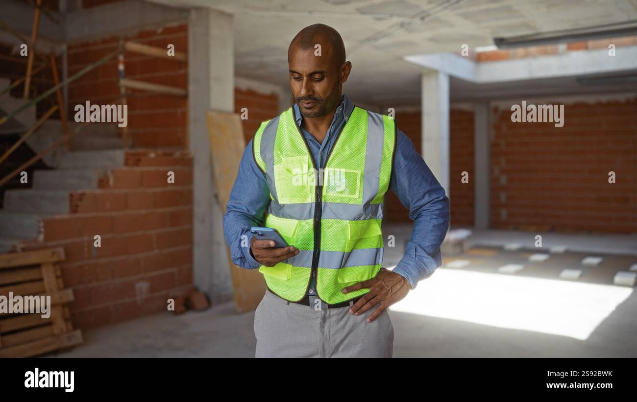 Young man in a high-visibility vest using a smartphone at a construction site showing him ...