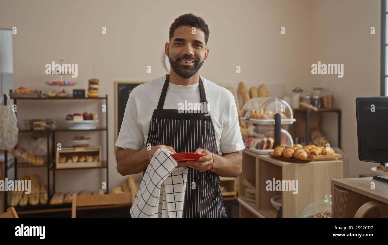Young man in bakery shop smiling while holding dish towel in modern ...