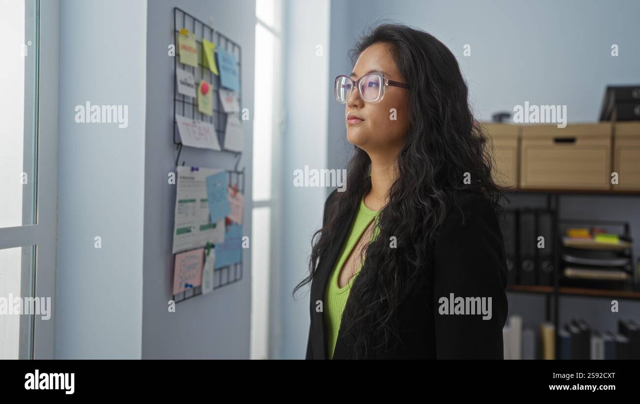 Woman standing in office wearing glasses looking at bulletin board with ...