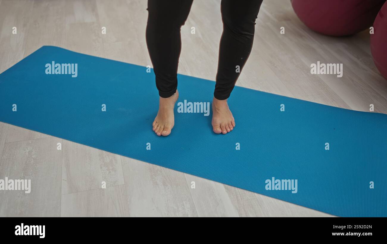 Woman standing barefoot on blue mat in gym interior focusing on balance ...