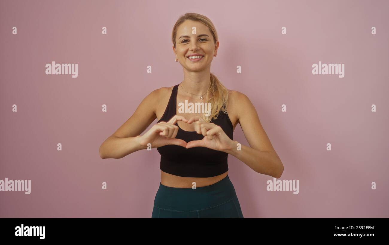Woman smiling on pink background with heart hand gesture, displaying ...