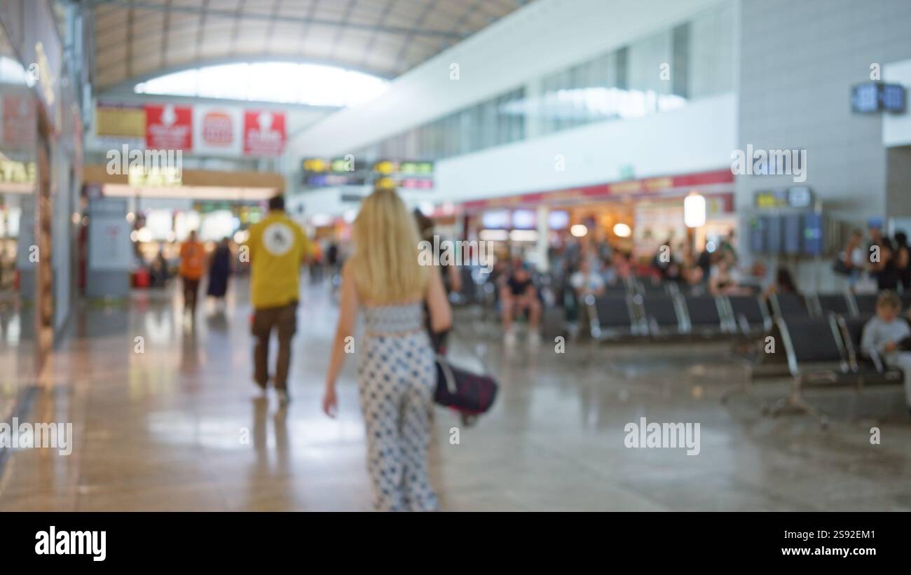 Woman walking through a busy airport terminal with people waiting in ...