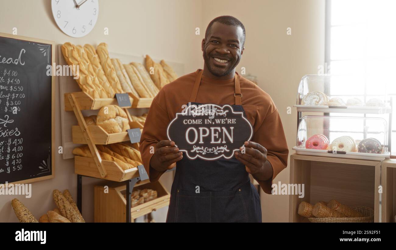Handsome young man in a bakery holding an open sign with various breads ...