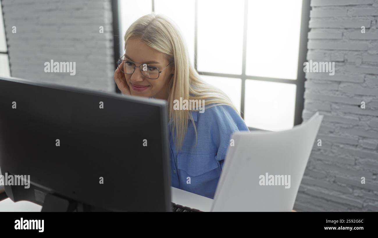 Woman working in a modern office, focused on a computer screen, holding ...
