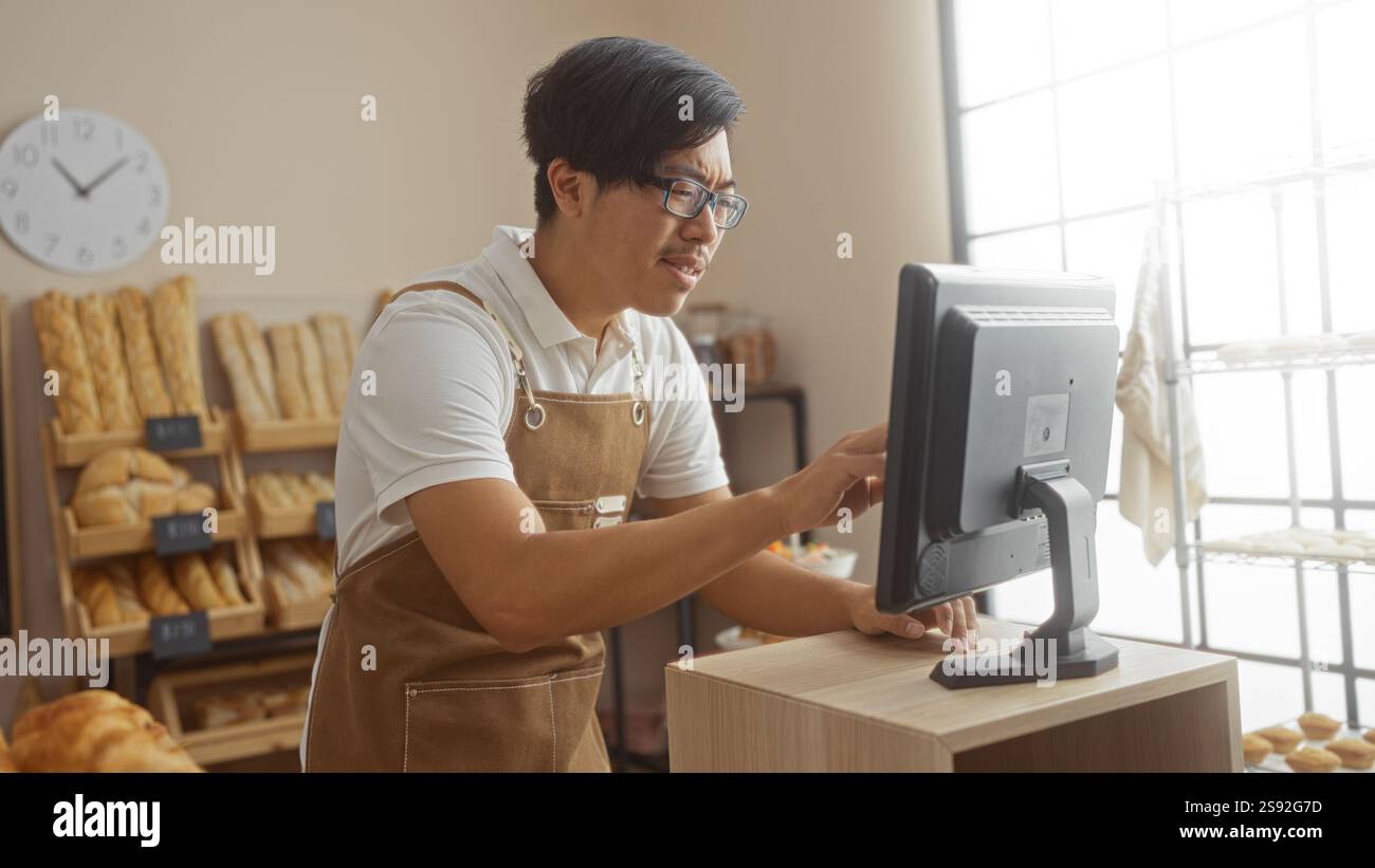 Young chinese man indoors working in a bakery, wearing an apron and ...