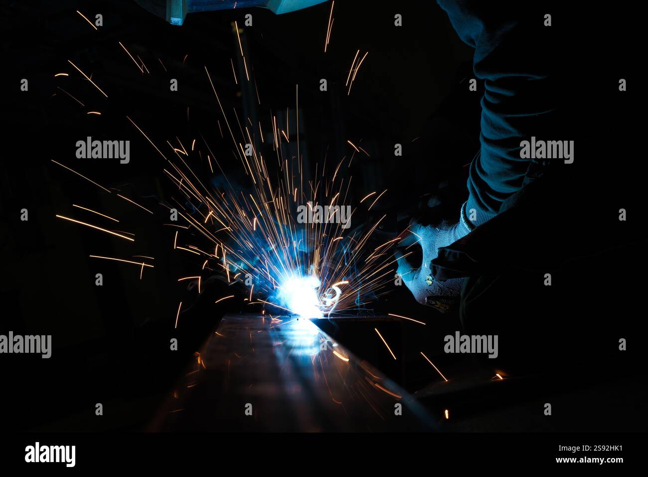 A person wearing a welding mask works on metal with a welding torch ...