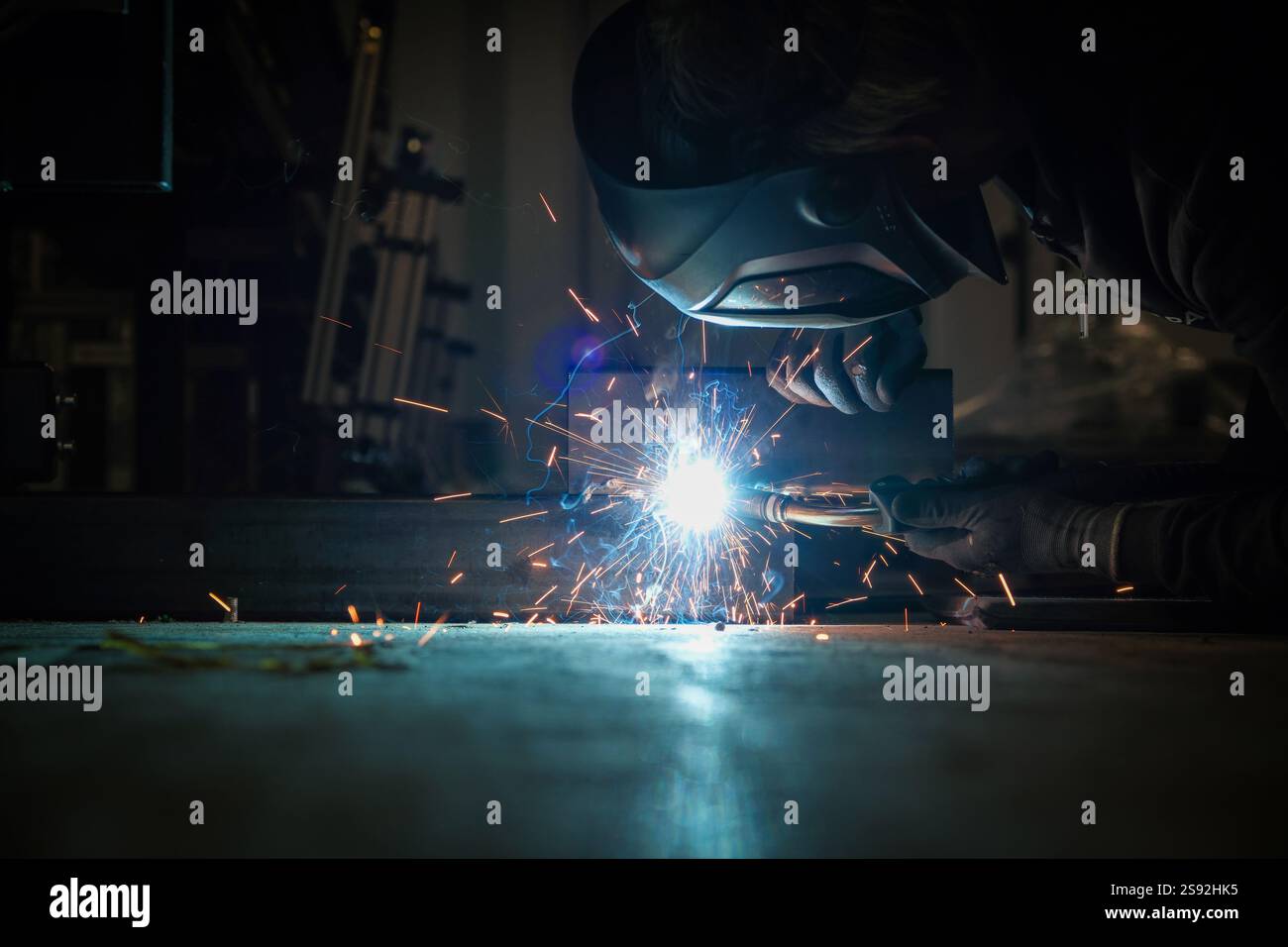 A person wearing a welding mask works on metal with a welding torch ...