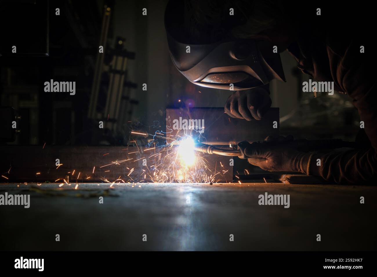 A person wearing a welding mask works on metal with a welding torch ...