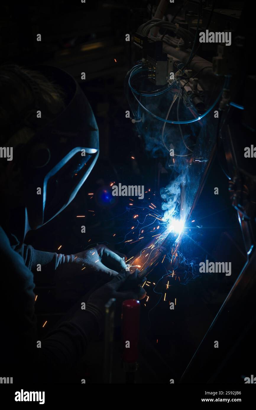 A person wearing a welding mask works on metal with a welding torch ...