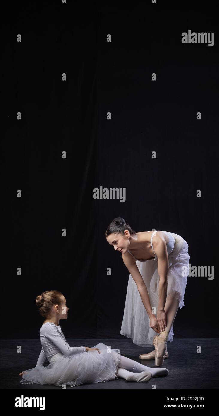 Adult ballerina bending to adjust pointe shoes, child sitting nearby ...