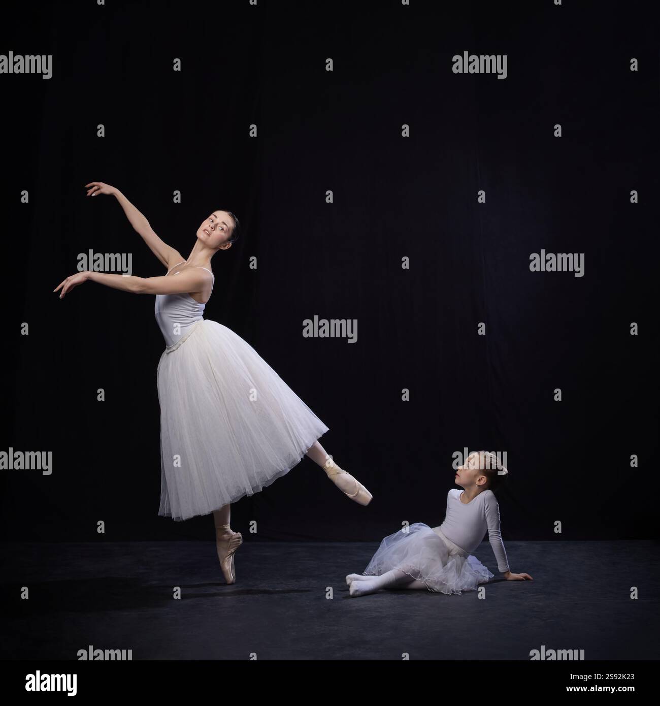Adult ballerina posing mid-dance with leg raised, child sitting on ...