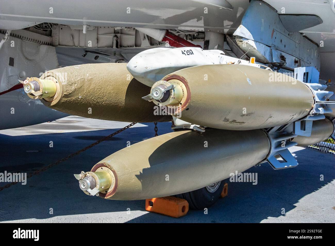 Three large bombs are on the ground next to a plane. The bombs are ...