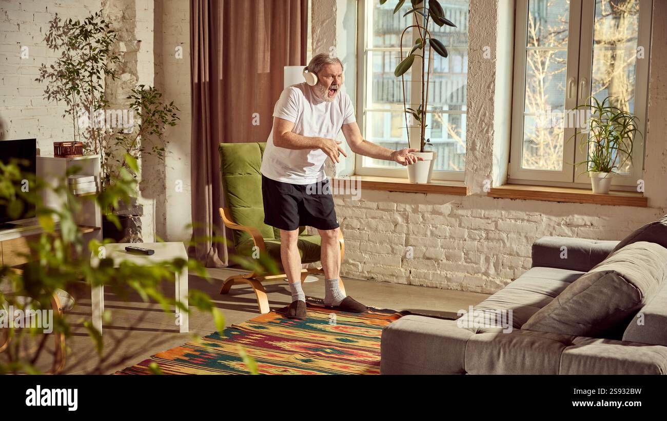 Elderly man in home wear listening to music in headphones and playing ...
