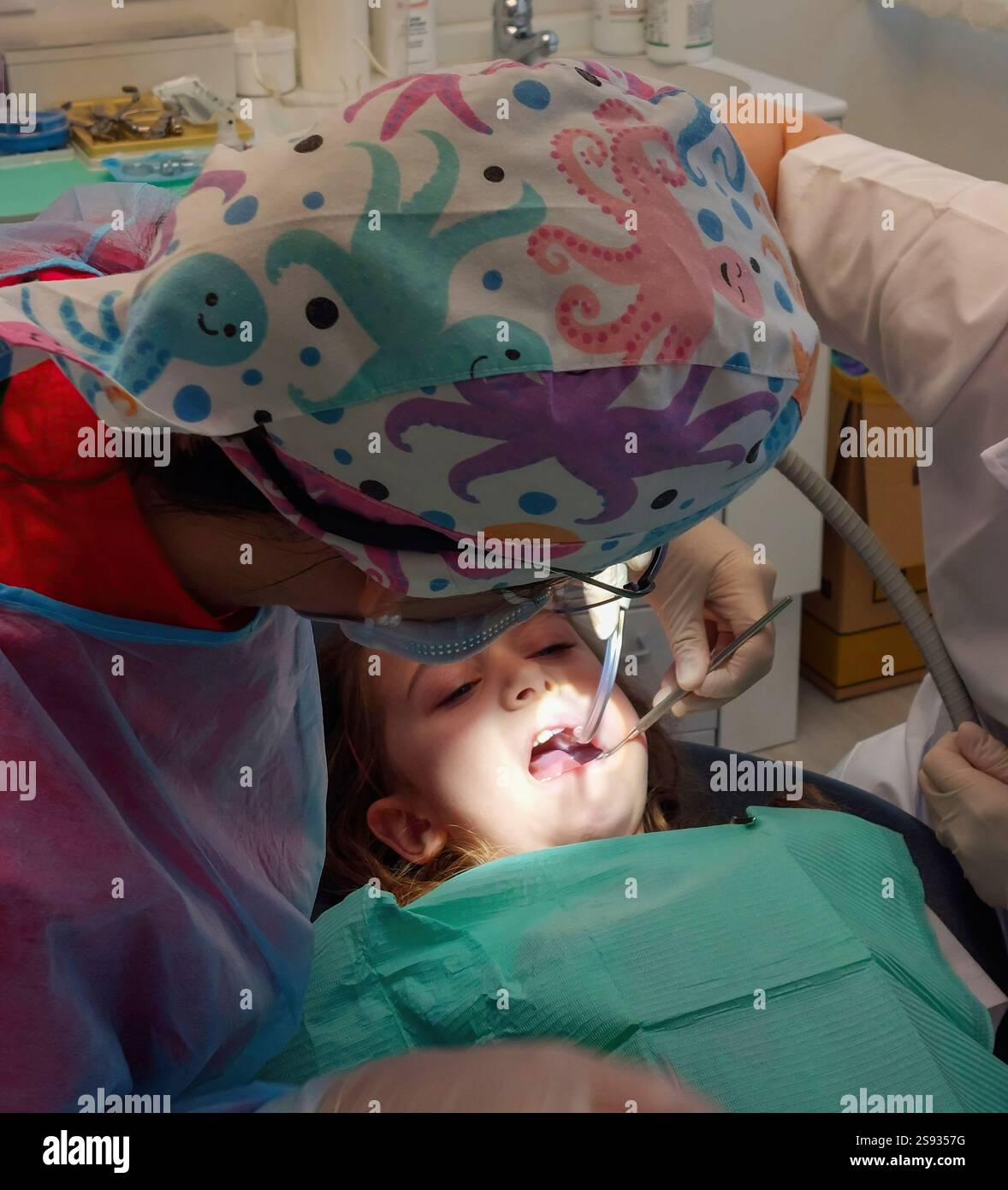 Dentist wearing colorful surgical cap using dental tools examining ...