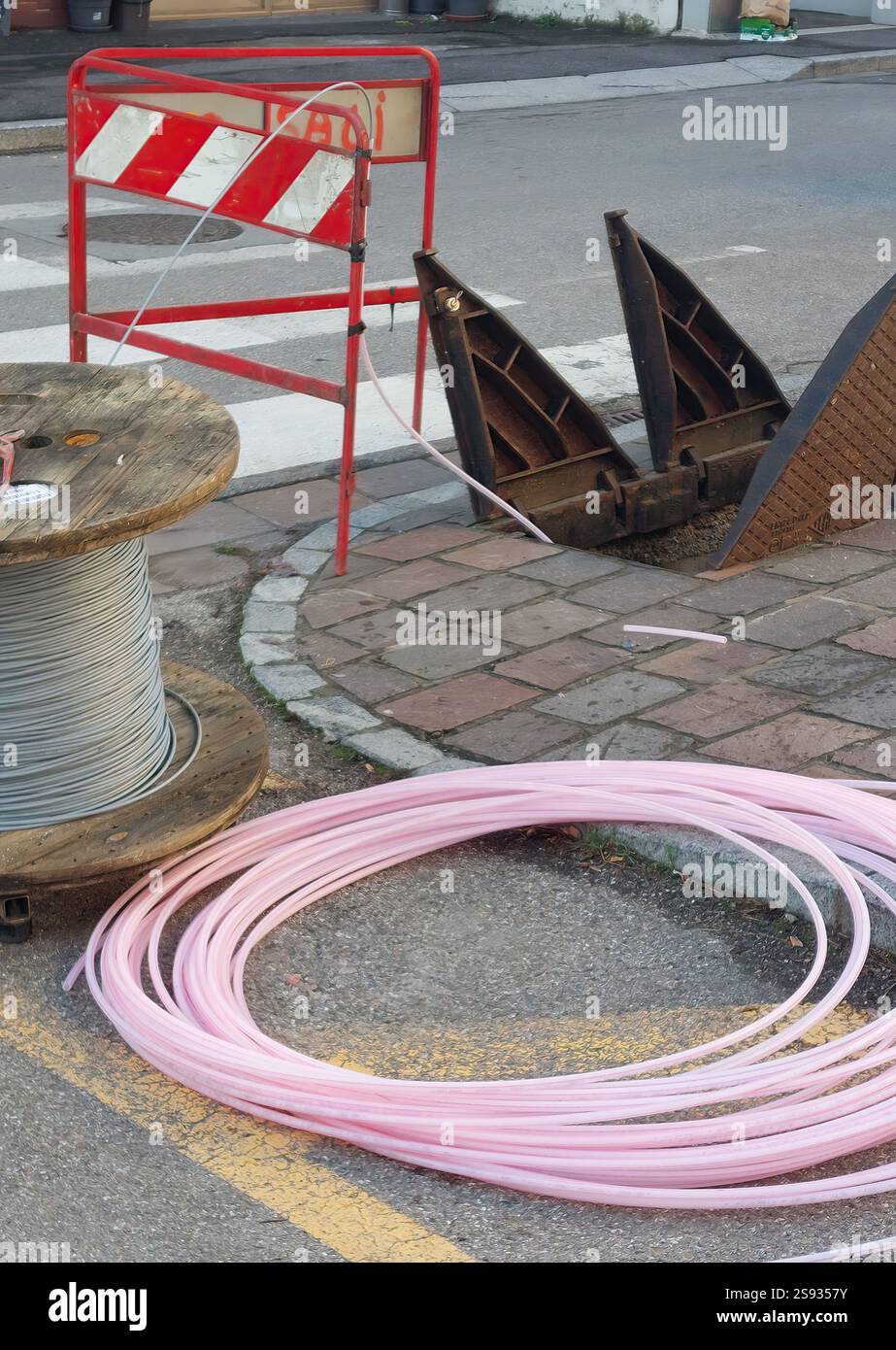 Pink fiber optic cable is being laid in a street near a sidewalk and a ...