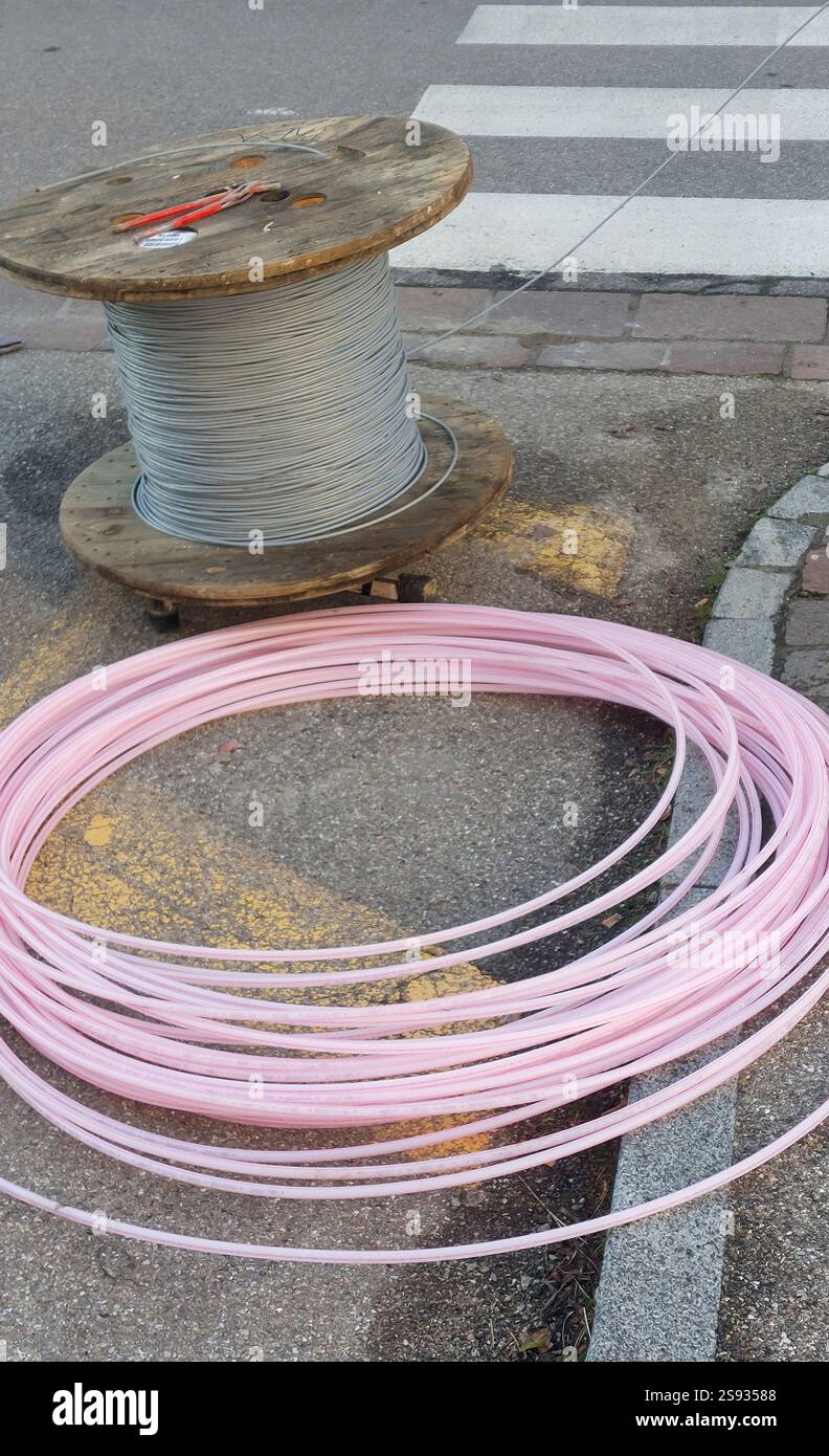 Pink fiber optic cable lying on the ground near a wooden spool with ...