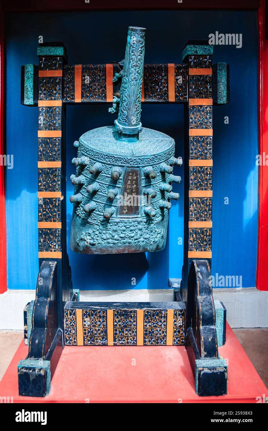 A large, ornate bell sits on a stand. The bell is made of bronze and ...