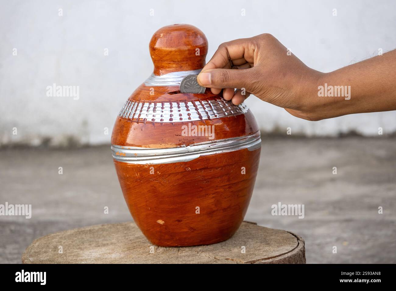 A female hand inserts a coin into a clay bank, illustrating the concept ...