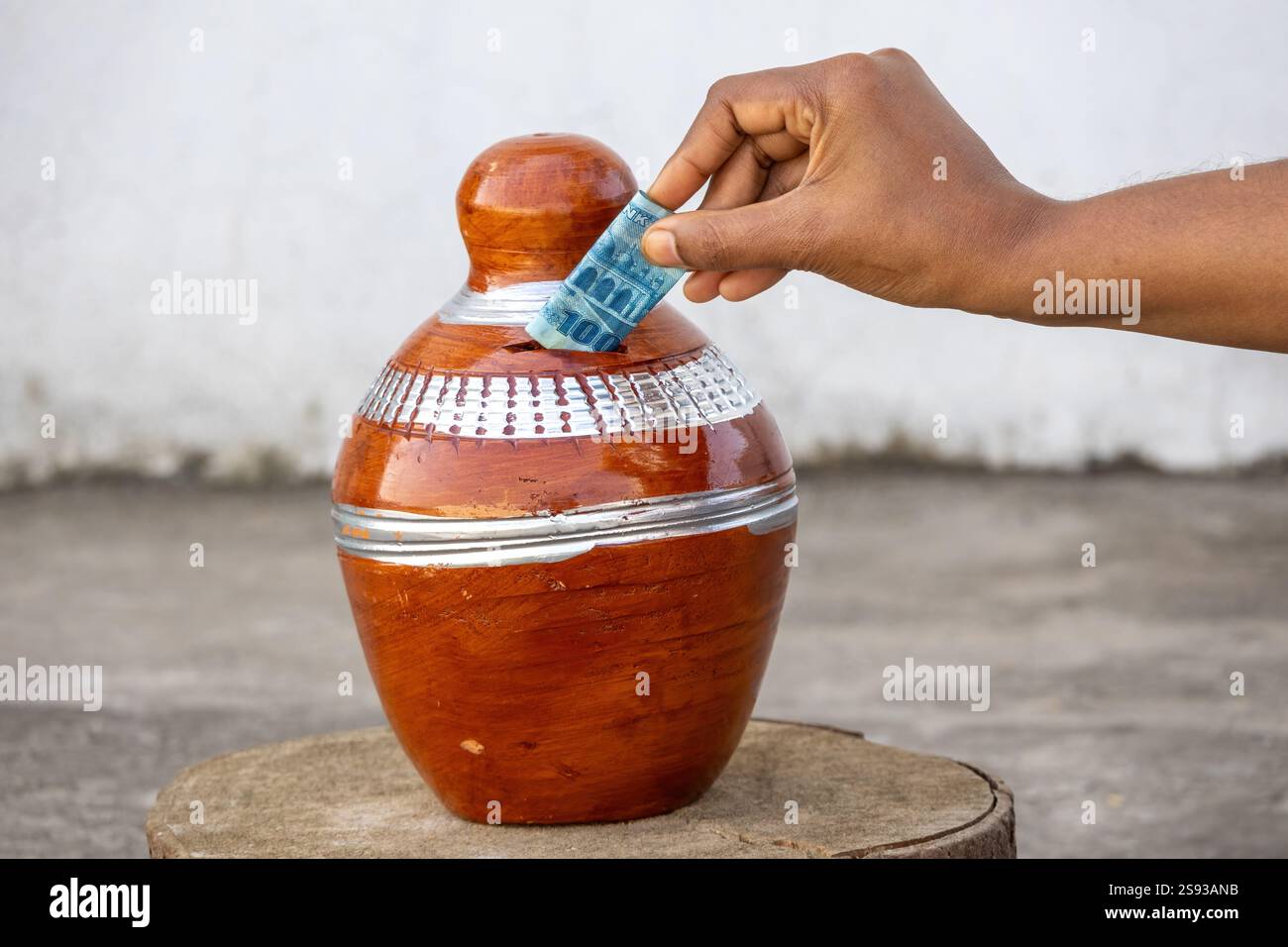 A female hand is depositing money into a clay bank, illustrating the ...