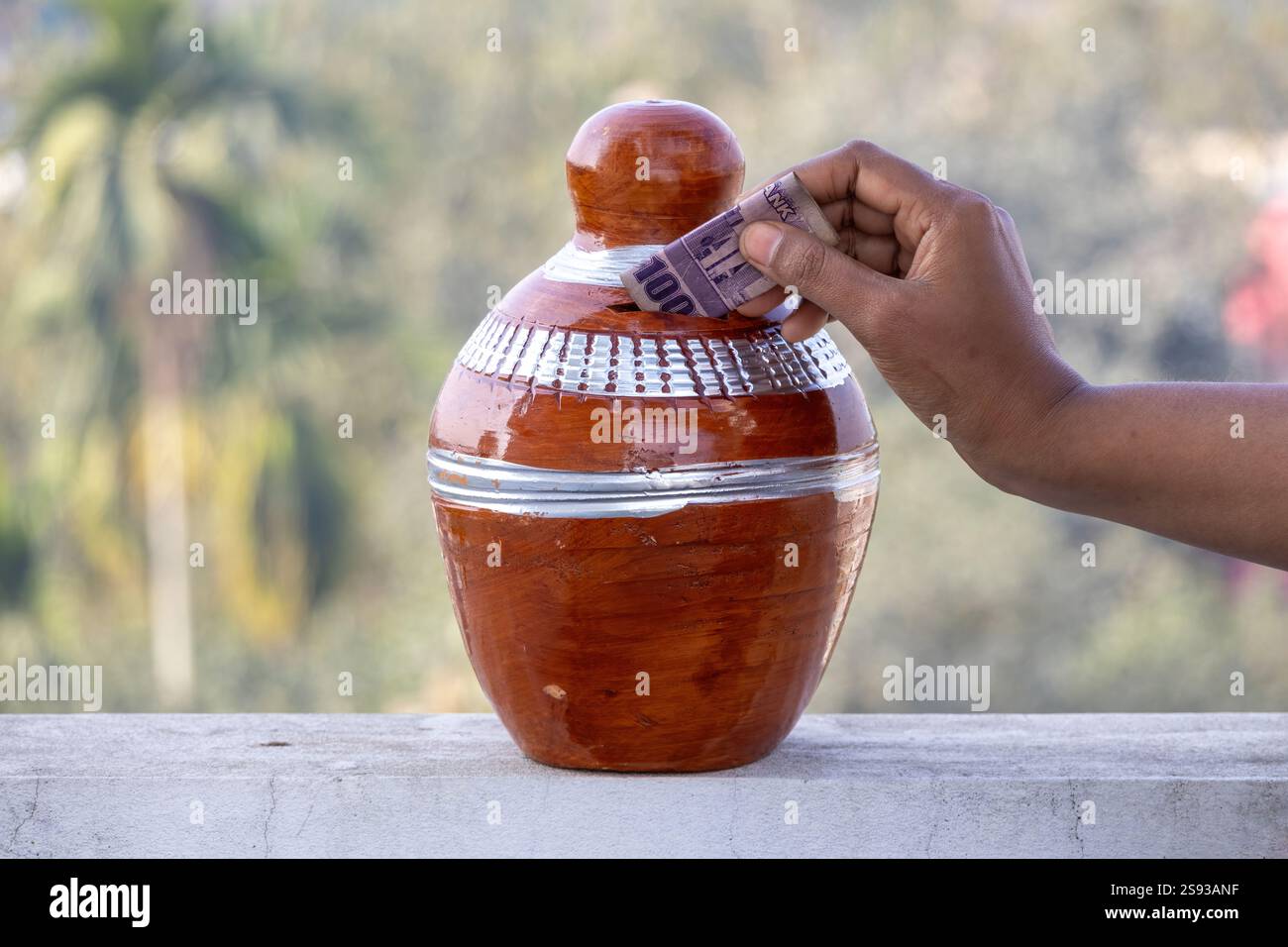 A woman's hand is putting money in a clay bank Stock Photo - Alamy