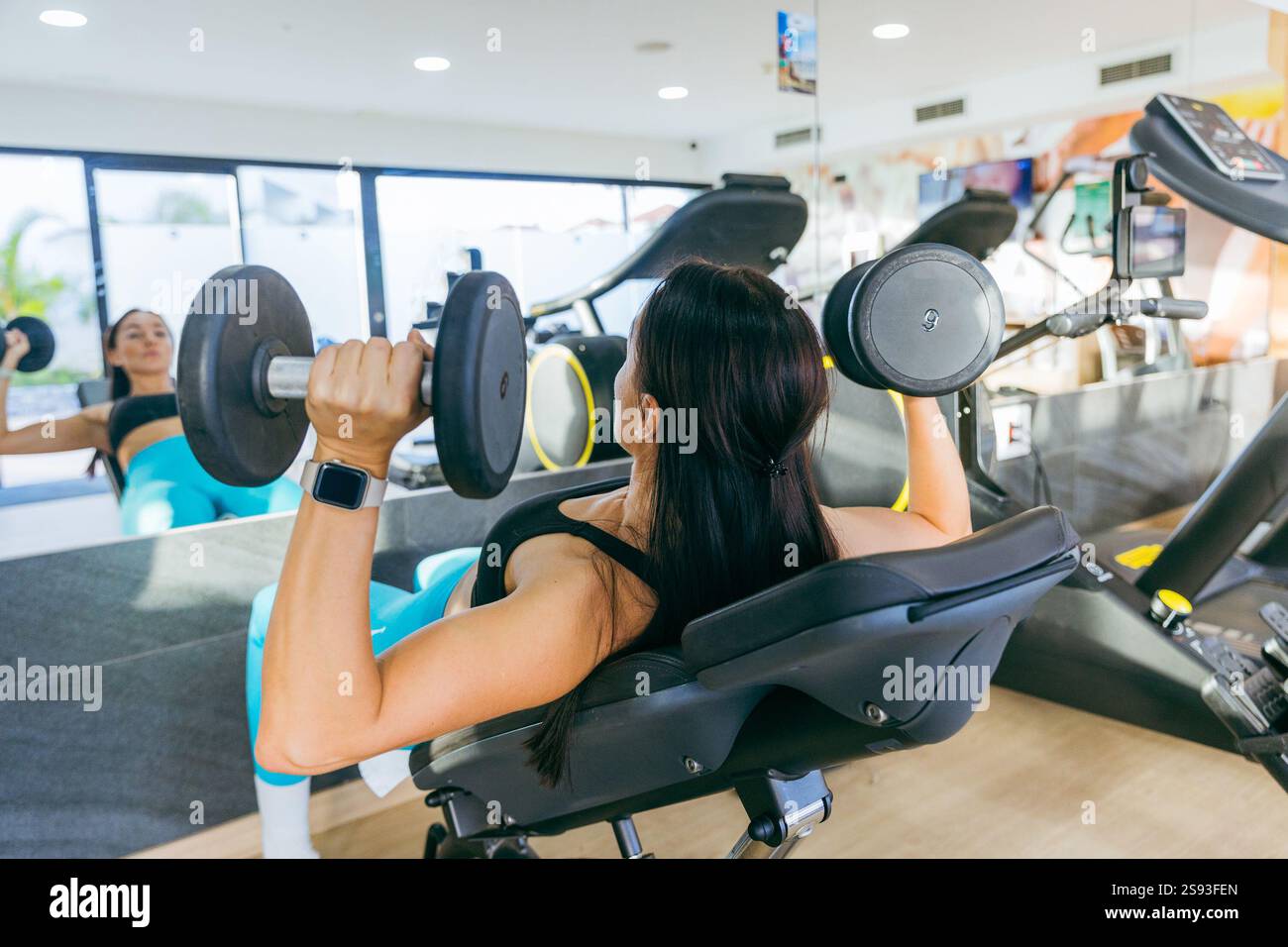 A brunette woman is lifting dumbbells in a gym, photo from behind with ...