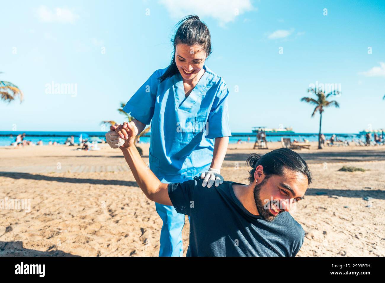A doctor in a blue scrubs is helping a man with his arm at the beach ...
