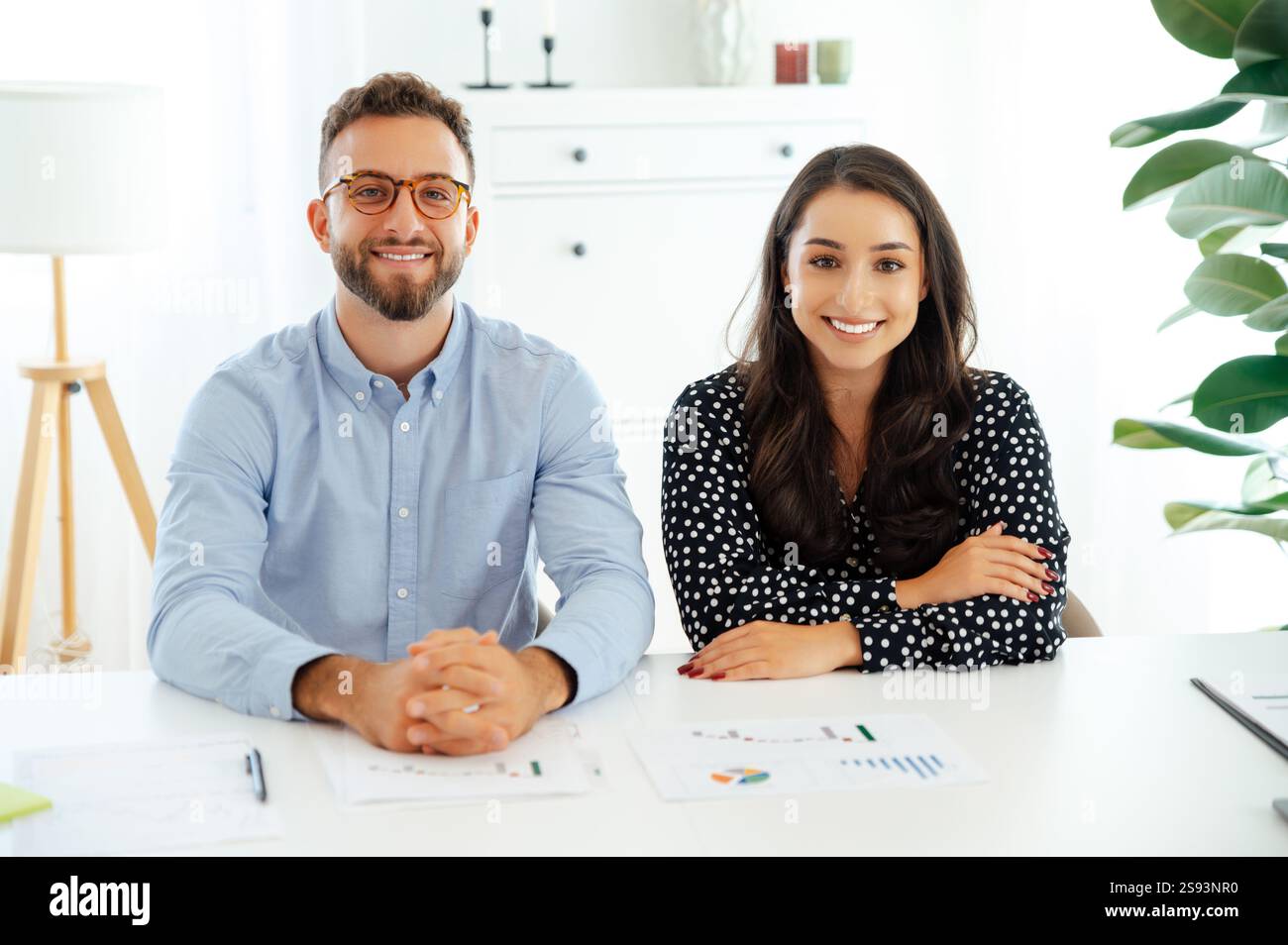Confident positive business partners sitting side by side at a desk ...