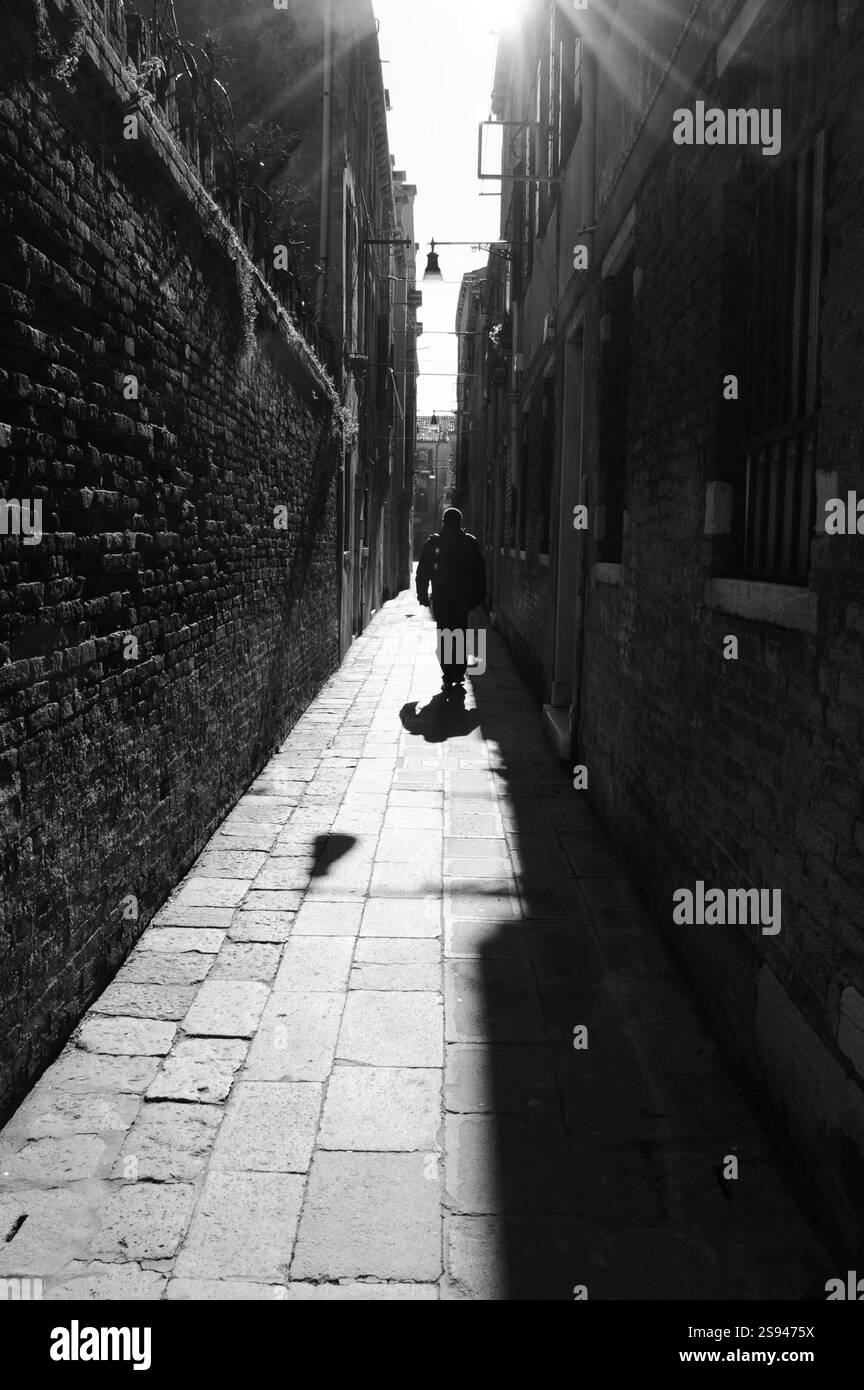 Silhouette of old man going on narrow street in shining sun rays ...