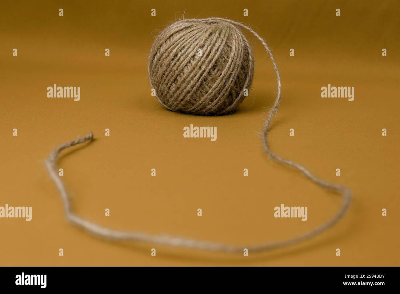 A ball of twine with a loose thread unraveling on a brown background ...