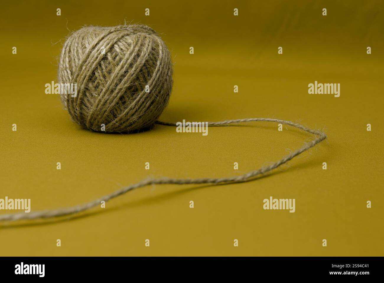 A ball of twine with an unraveling thread placed on a green background ...