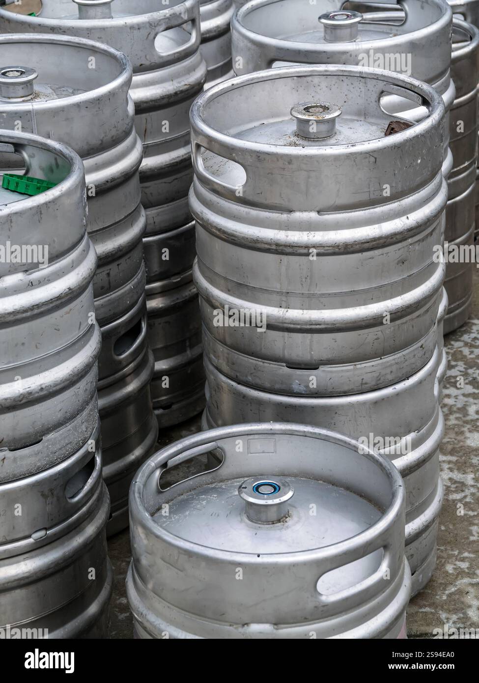 A collection of stainless steel beer kegs stacked outdoors in a storage ...