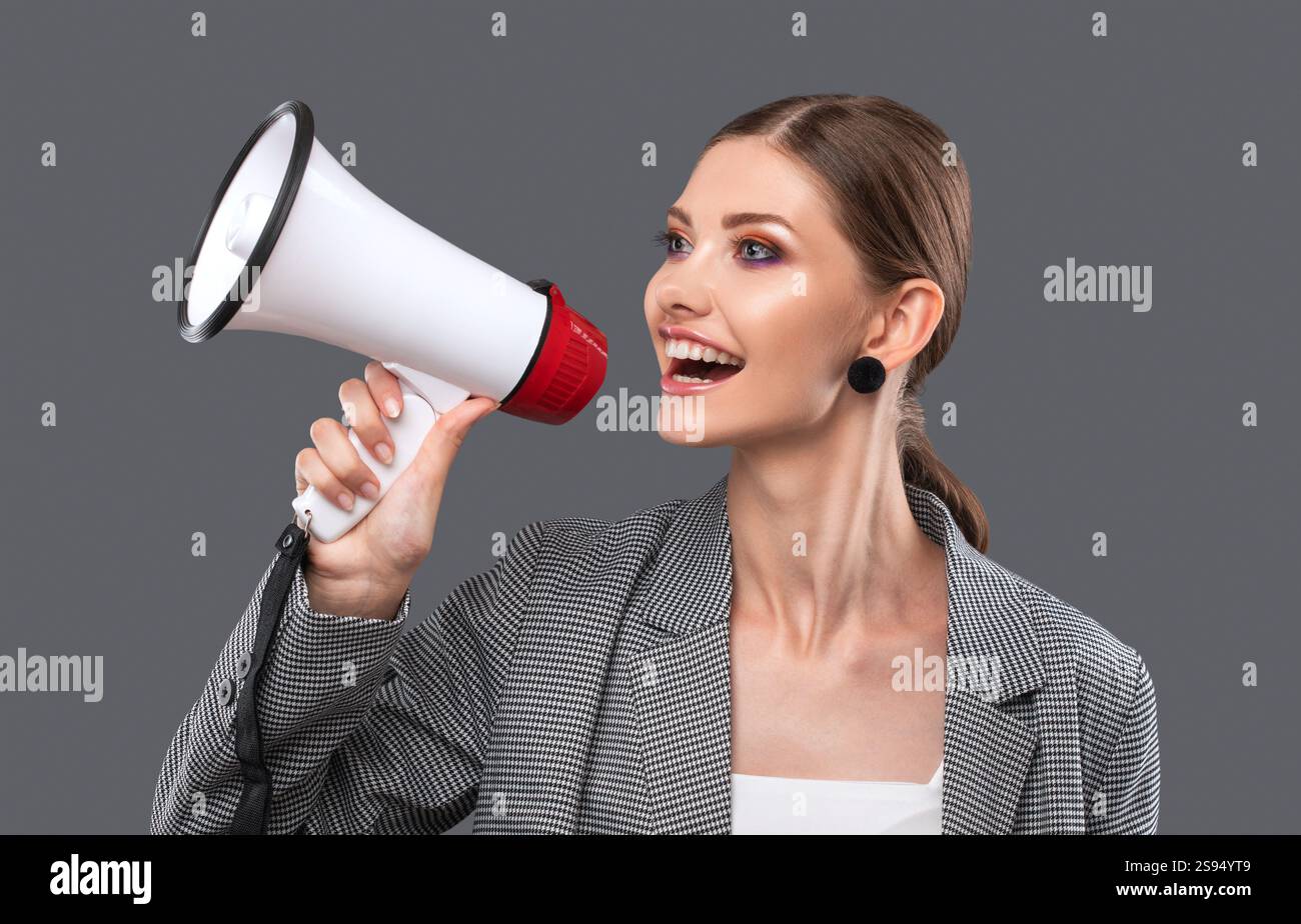 A beautiful joyful girl shouts into the loudspeaker on isolated pink ...