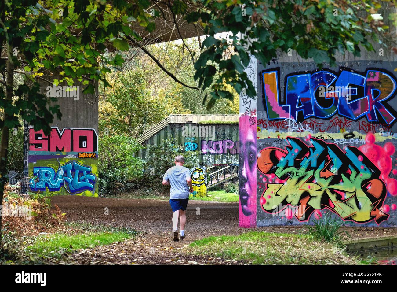 Male runner passing by colourful graffiti painted on concrete columns ...