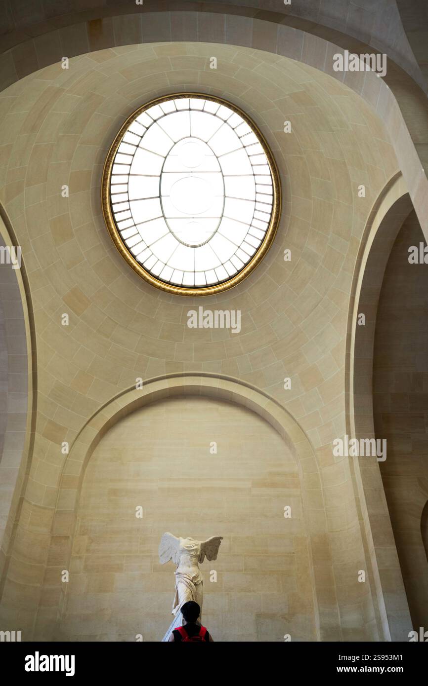 Sunlight streams through a circular window above Samothrace; a headless ...