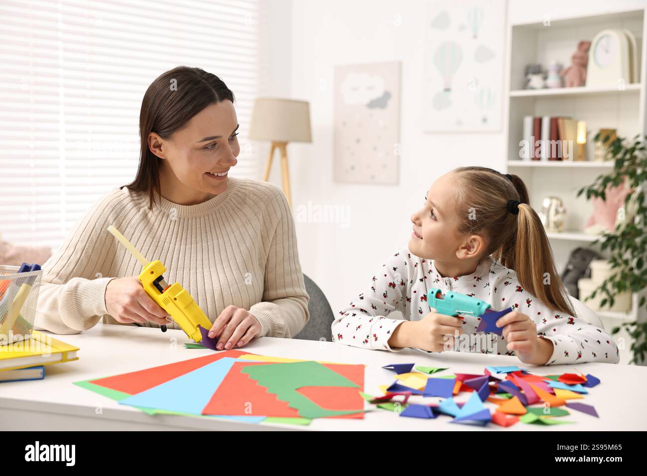 Mother and daughter with hot glue guns and color paper making craft at ...
