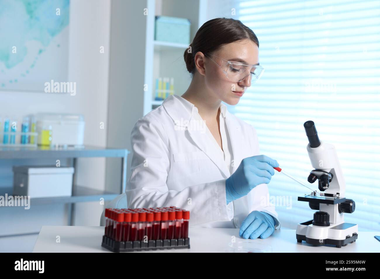 Laboratory testing. Doctor dripping blood sample onto glass slide while ...