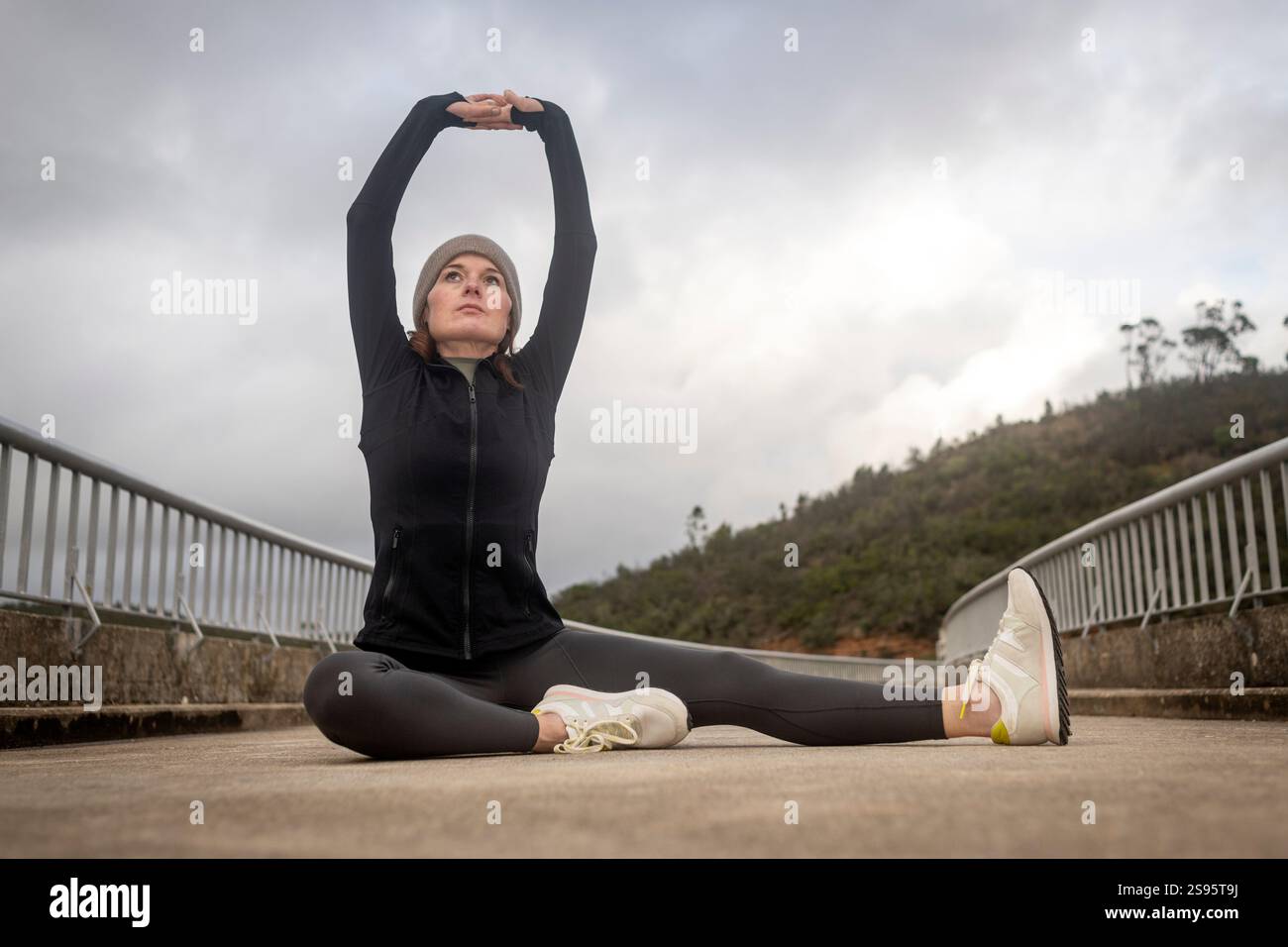 woman runner sitting in road stretching, arms above head Stock Photo ...