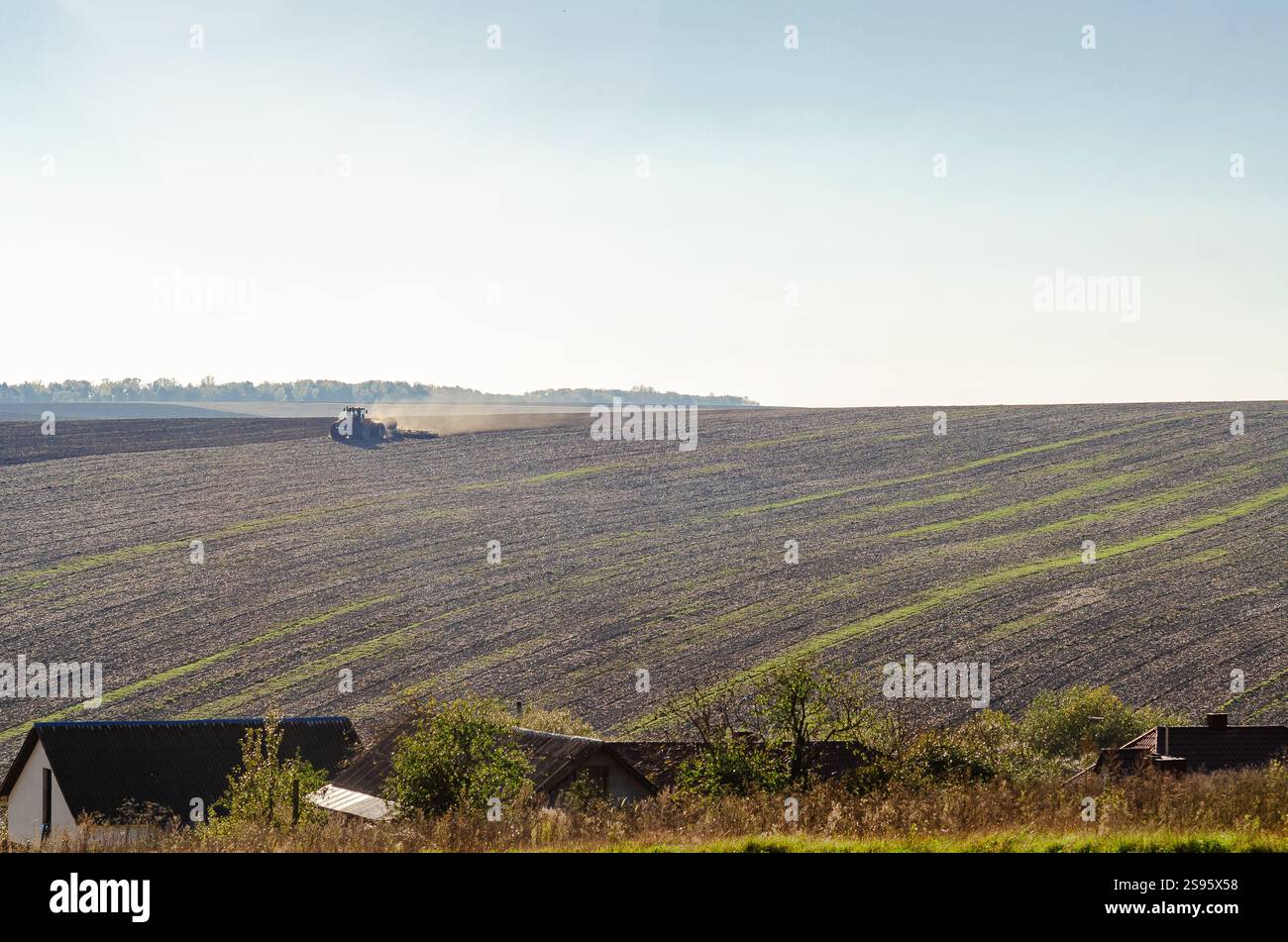 Tractor plows field, raising dust, turning over black soil in ...