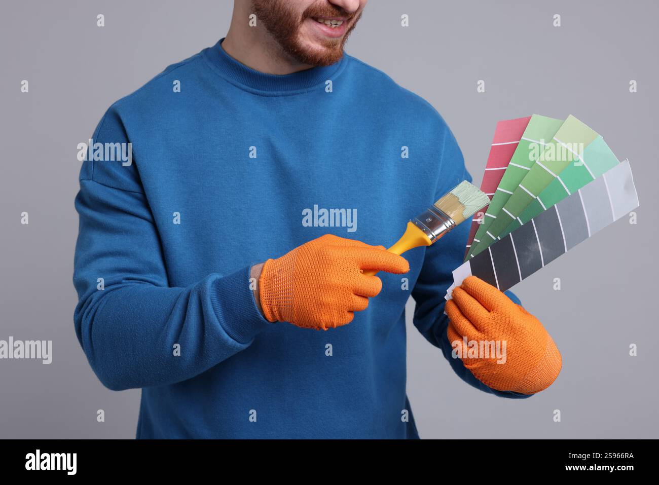 Man with paintbrush and color selection chart on light grey background ...